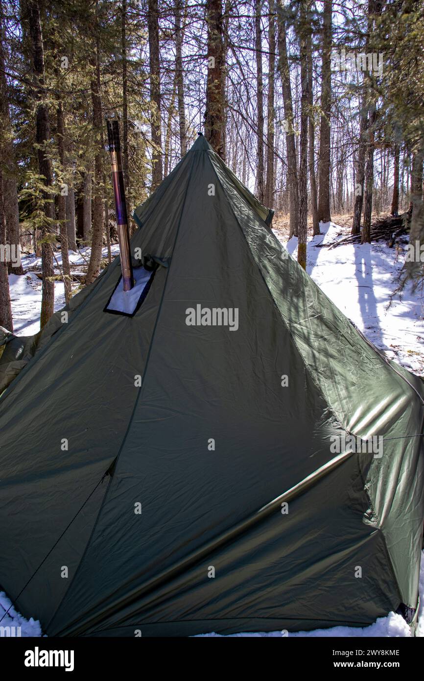 This image depicts a teepee tent set up in a snowy landscape, with a ...