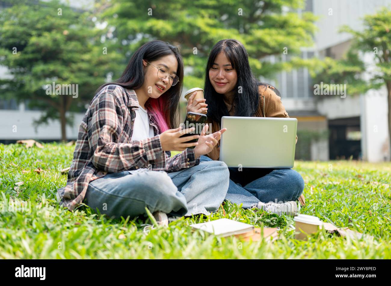 Two happy young Asian female college students are sitting on grass in a ...