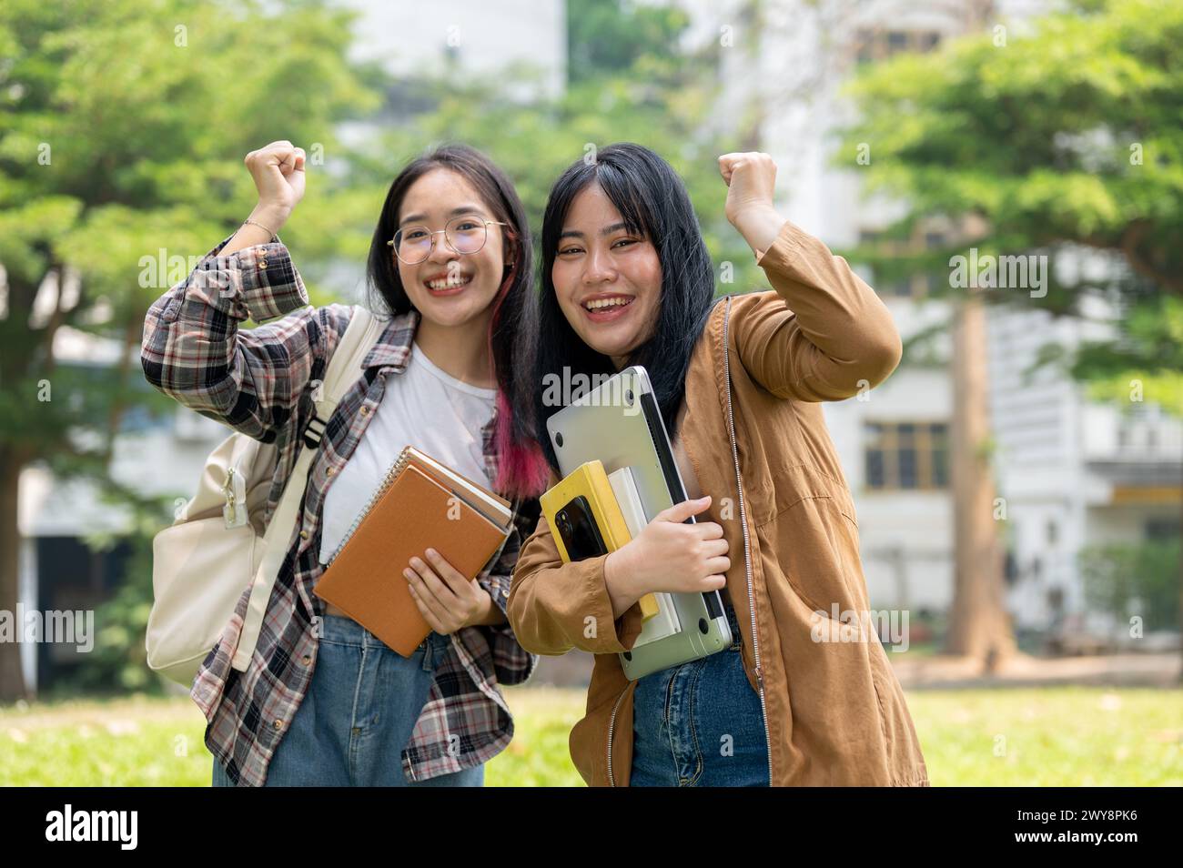 Two excited young Asian female college students are raising their fists ...