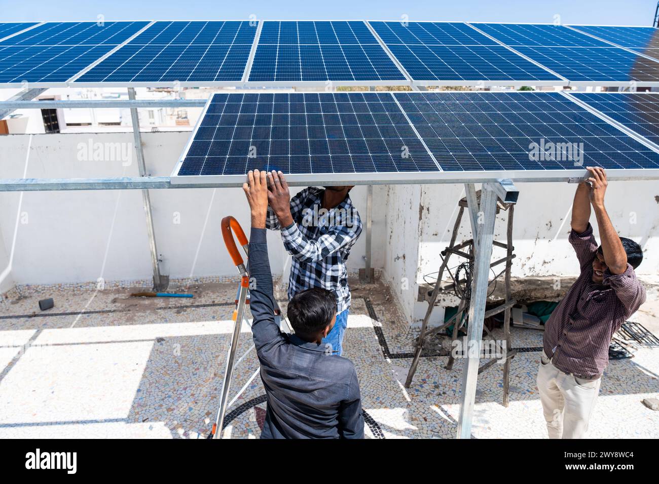 Indian workers installing solar panels on roof of house. Maintenance of photovoltaic panel ...