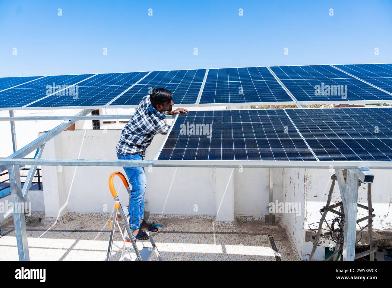Indian worker installing solar panels on roof of house. Maintenance of ...