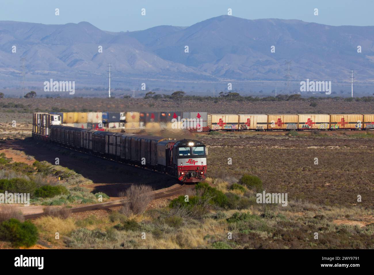 Freight train hauling cargo containers through a desert with mountains ...