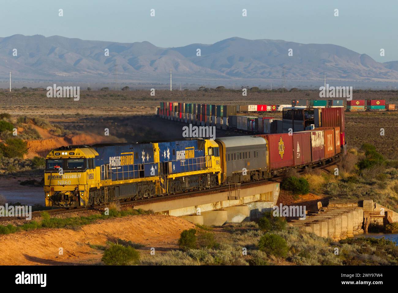 Freight train hauling cargo containers through a desert with mountains ...