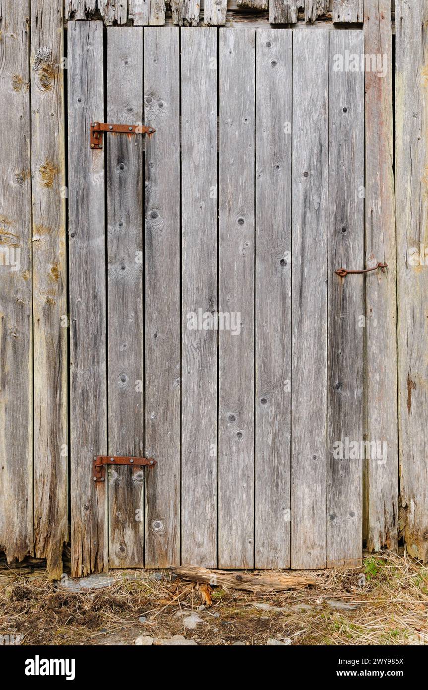 Aged wooden planks form a barn door with rusty metal hinges and latch, conveying a sense of ...