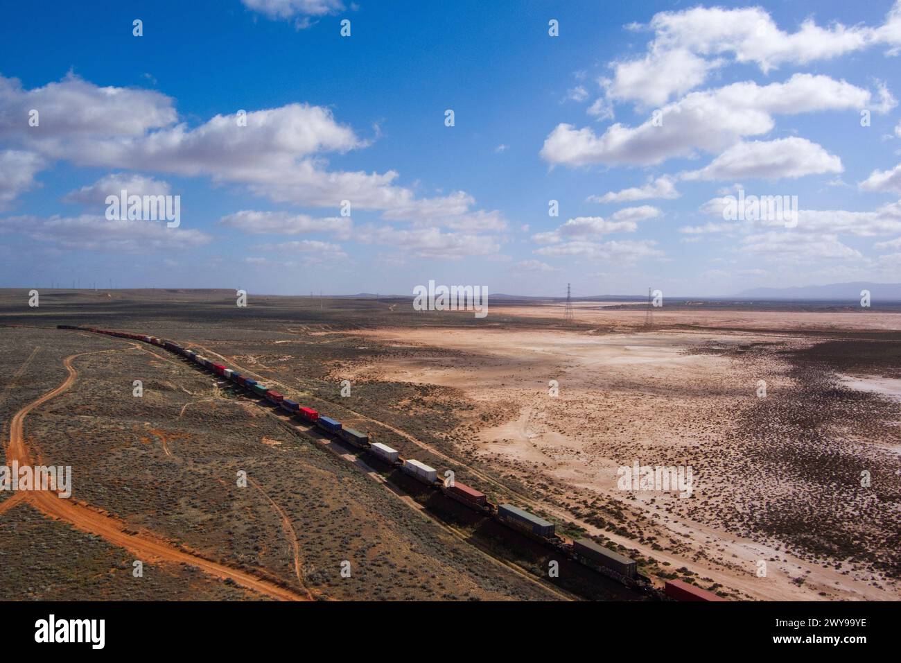 Aerial view of a long freight train moving through a vast, arid desert ...