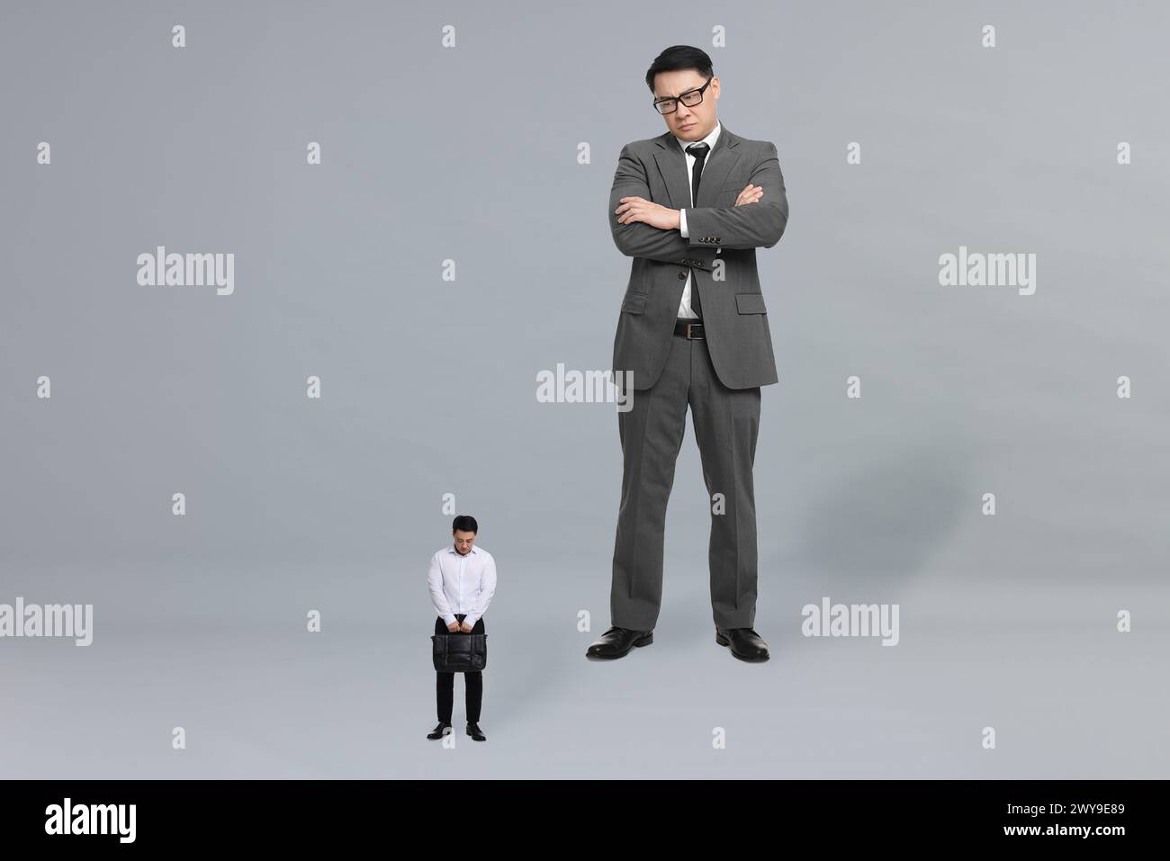 Giant boss and sad small man on grey background Stock Photo - Alamy