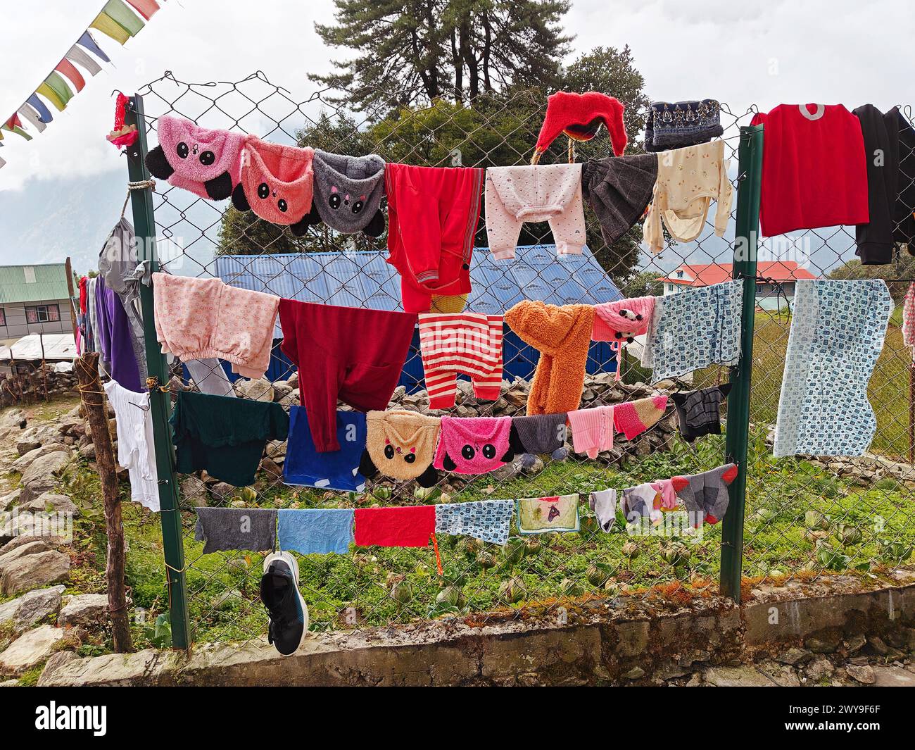 Colorful clothes hanging on a wire fence with prayer flags and trees in ...