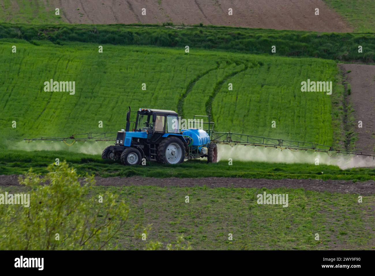Aerial view of tractor spraying crop in green farm fields with ...