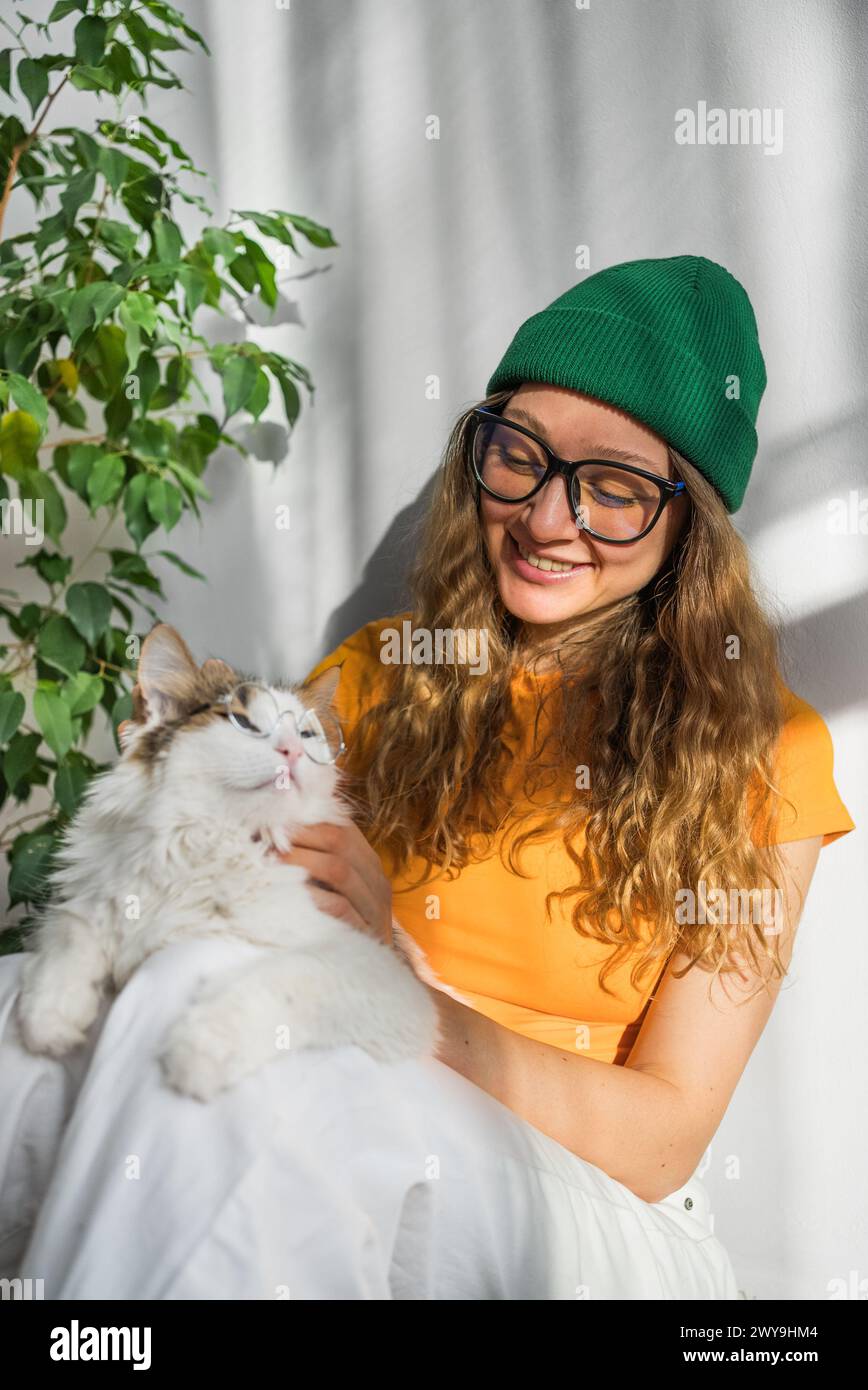 A cheerful young woman in a green beanie lovingly cradles her fluffy ...