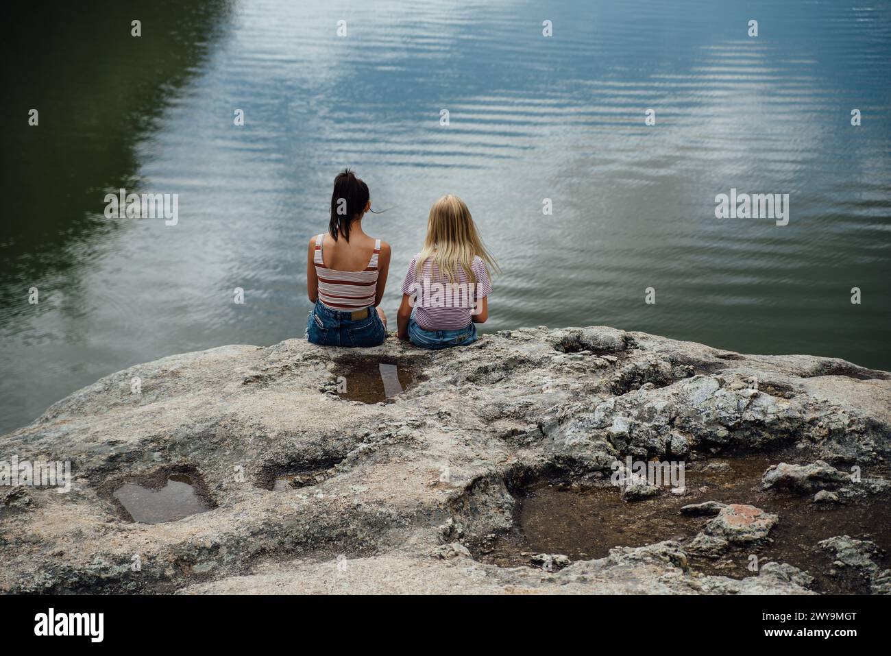 Wide rear view of two teen girls sitting on rocks near a lake Stock ...