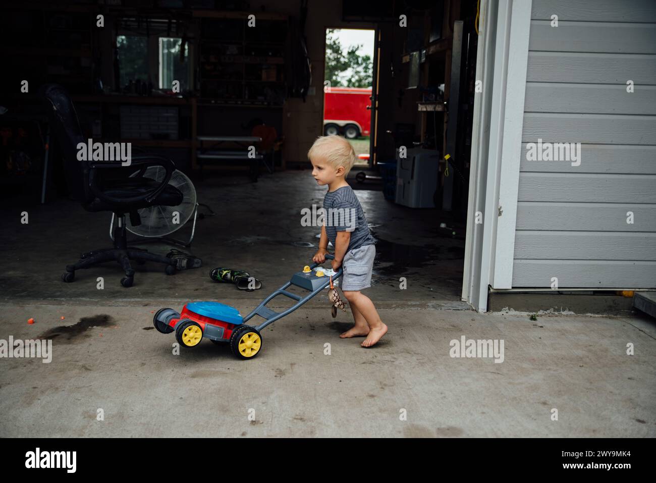 Small boy pushing toy lawn mower in front of garage outdoors Stock ...