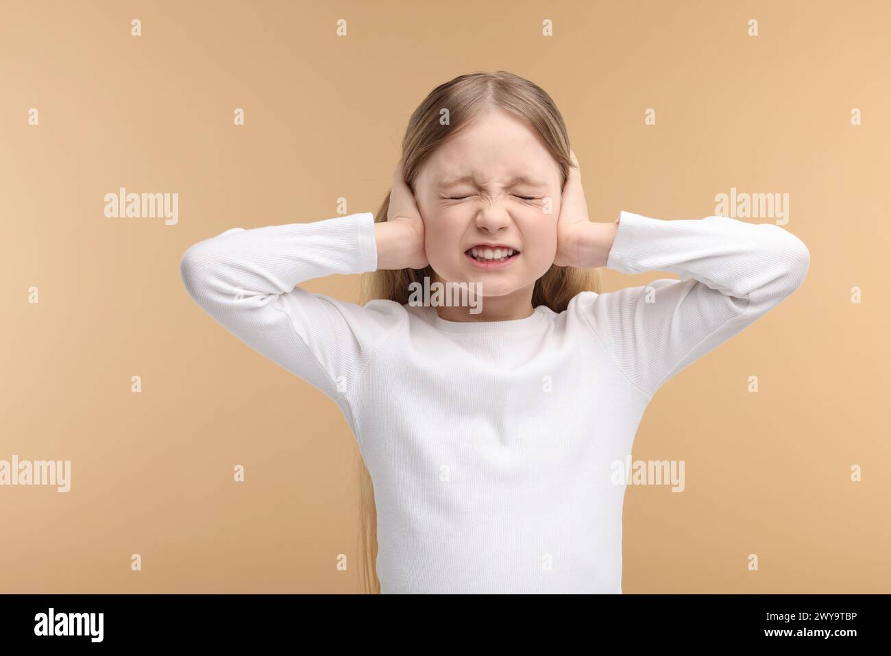 Hearing problem. Little girl suffering from ear pain on pale brown ...