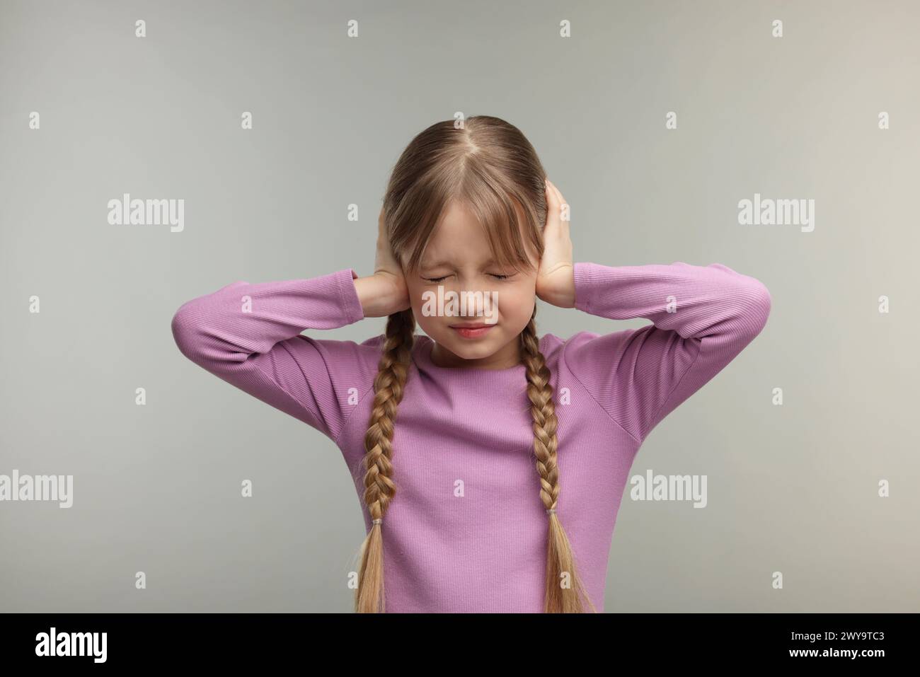 Hearing problem. Little girl suffering from ear pain on grey background ...