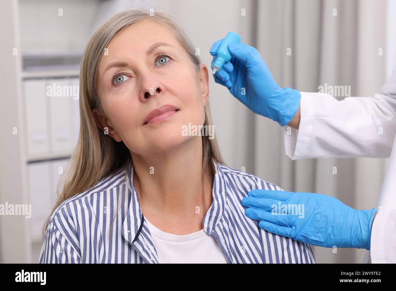 Medical drops. Doctor dripping medication into woman's ear indoors ...