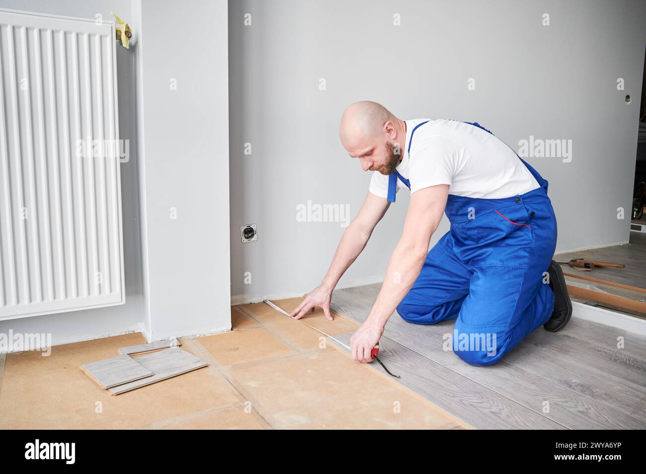 Man in work overalls measuring distance from wall to laminate board ...