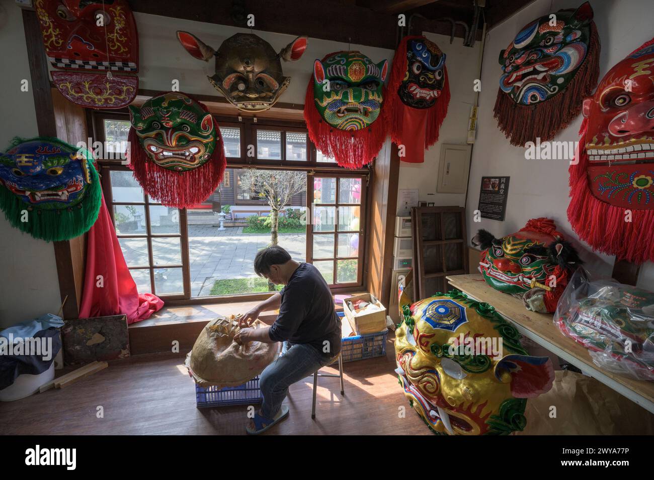An artisan is hand making a Chinese mask in a sunlit workshop ...