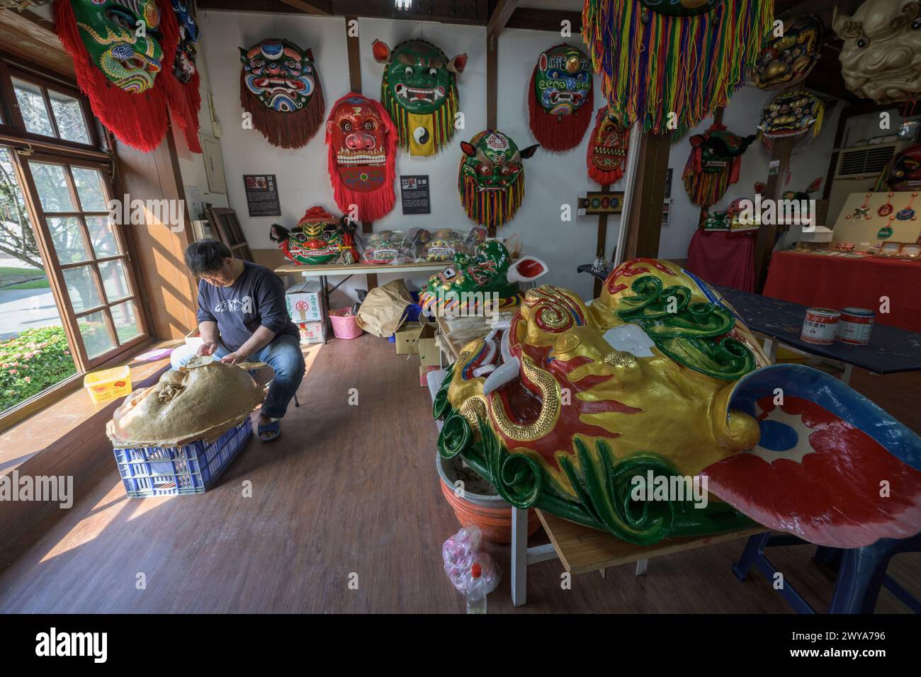 An artisan is hand making a Chinese mask in a sunlit workshop ...