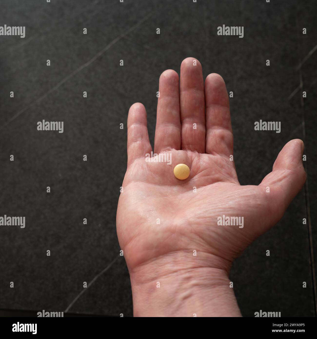 Hand holding a pill in the palm and presenting it. Black background ...