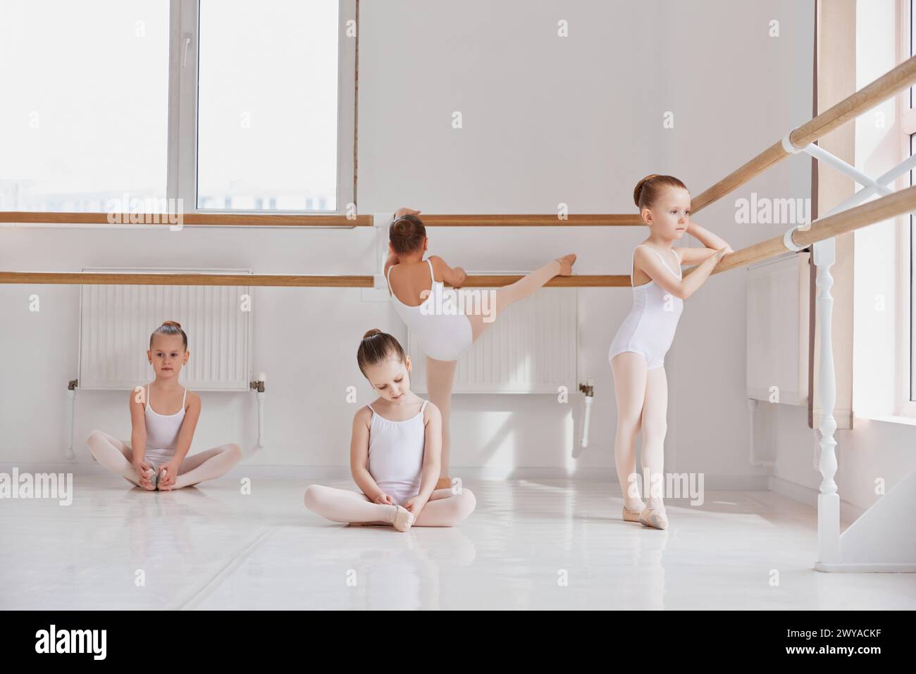 Four young ballet dancers practicing in a dance studio with barres and ...