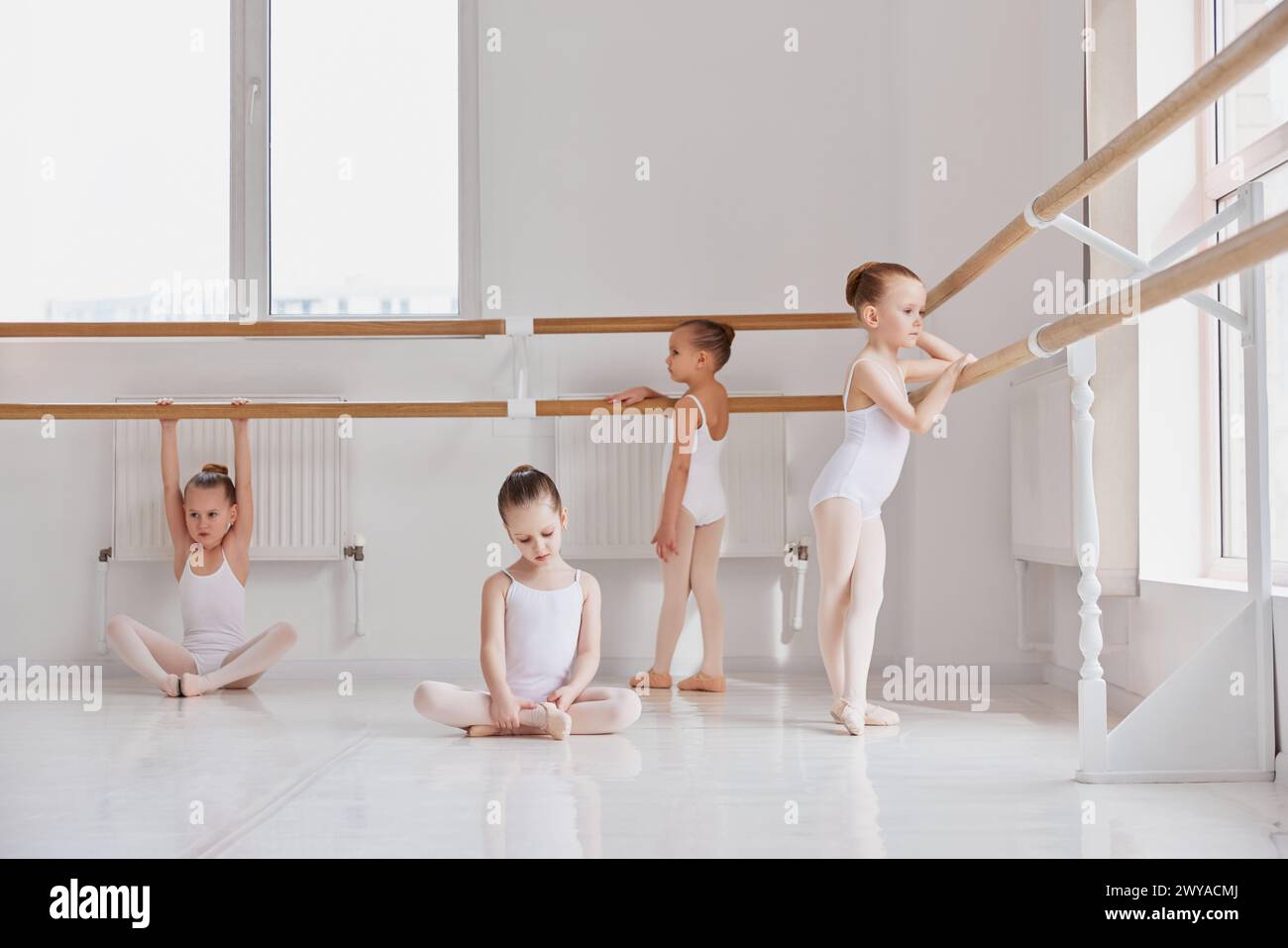 Group portrait of little girls in leotards ballet students stretching at barre in sunlit dance ...