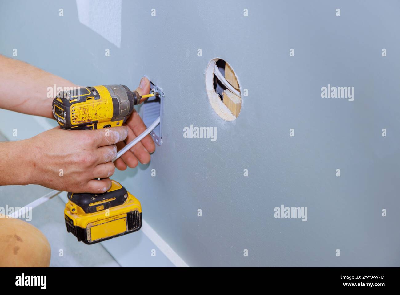 Professional electrician installing an electric socket in wall of ...