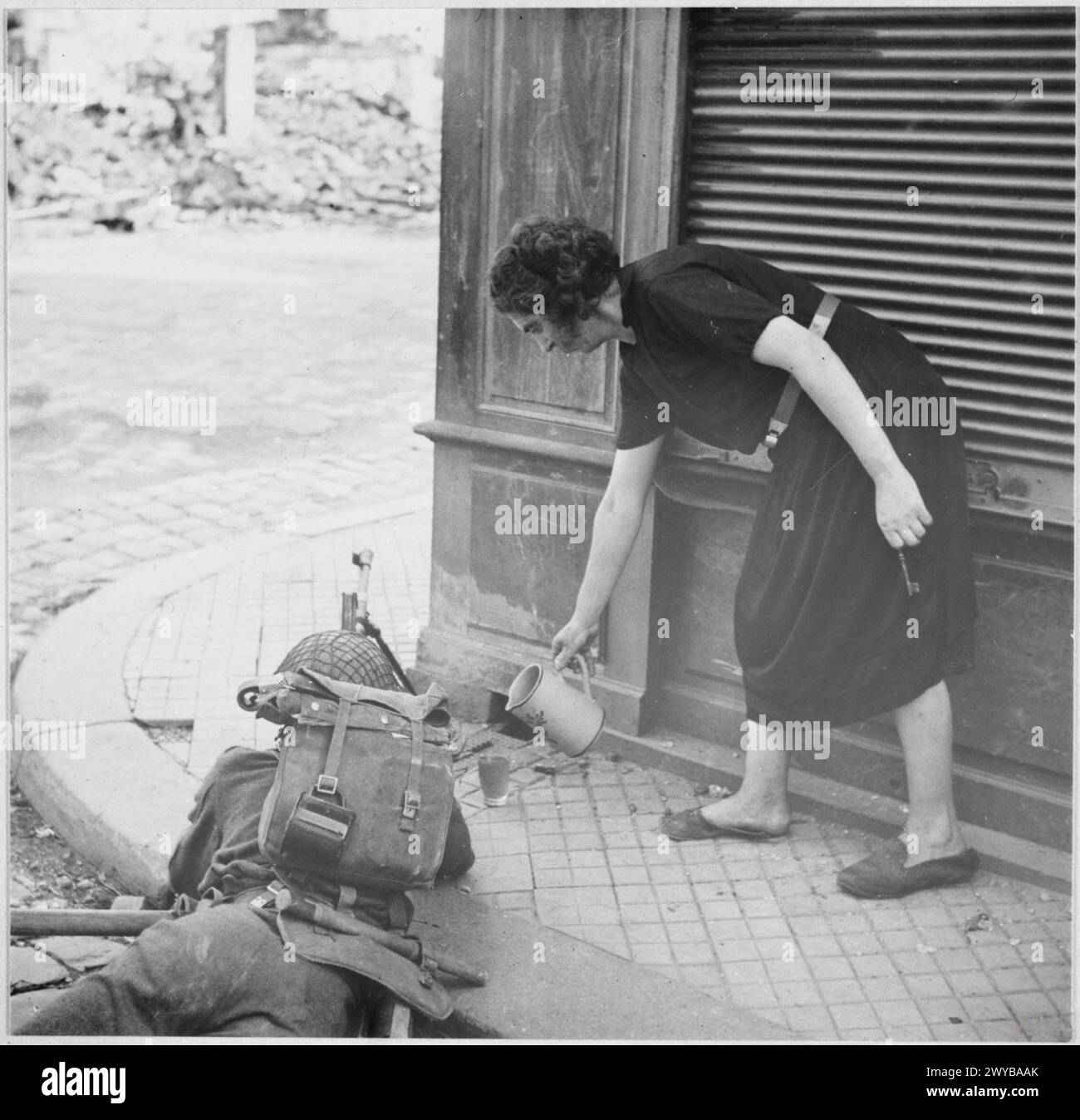 A civilian woman offers cider to a British Bren gunner in action at ...