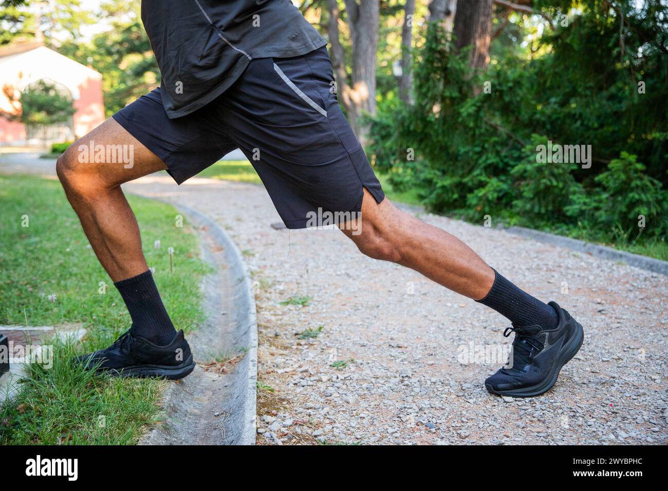 A man is stretching his legs on a sidewalk. He is wearing black shorts ...