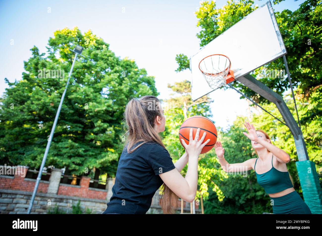 Two women playing basketball in a park. One of them is holding a ...