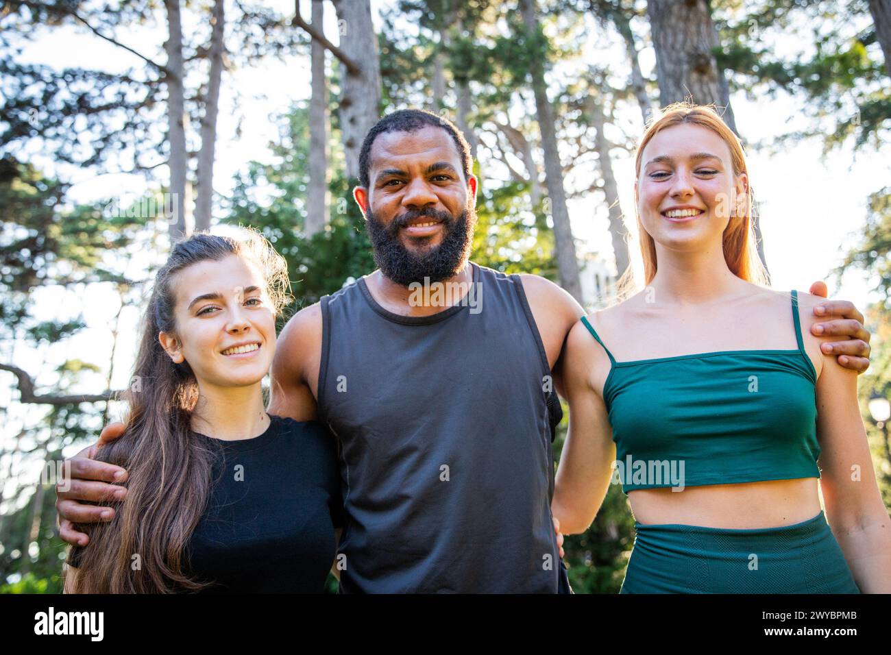 Three people are standing in a forest, smiling and posing for a picture ...