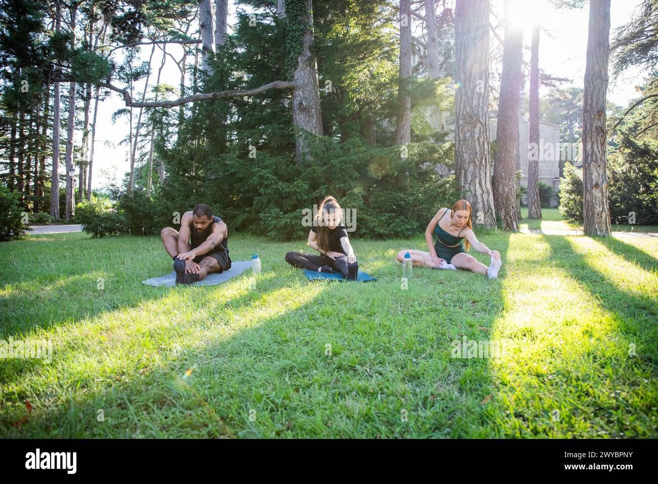 Three sporty people in a public park during a work out are stretching ...