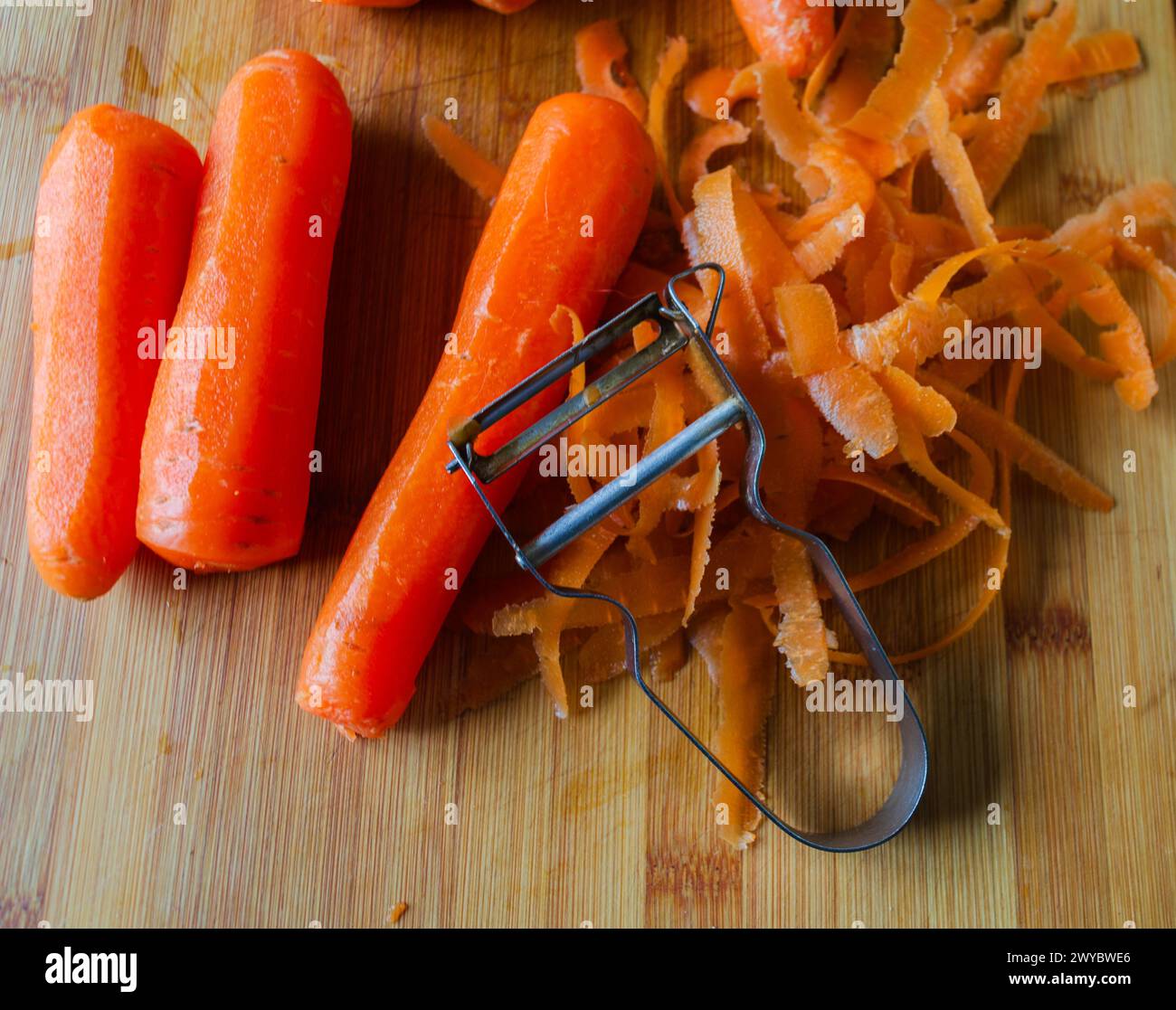 Chopped and peeled carrot with a peeler on a wooden chopping board ...