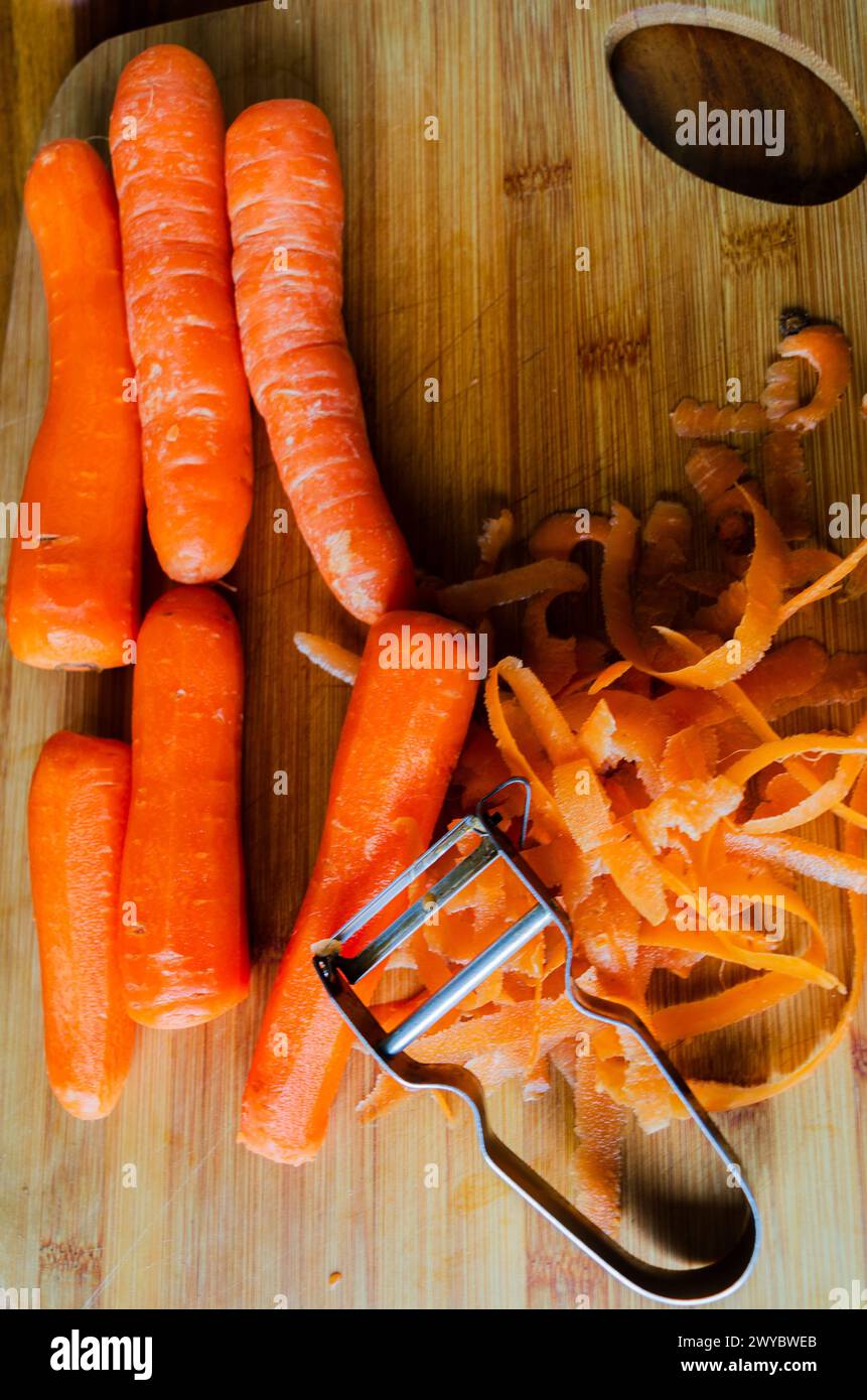 Chopped and peeled organic carrots with a peeler on a wooden chopping ...