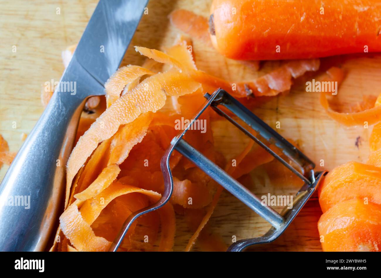 Chopped and peeled carrot with a peeler and knife on a wooden chopping ...