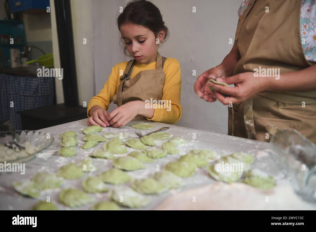 Portrait Caucasian little child girl helping her mom in the kitchen ...