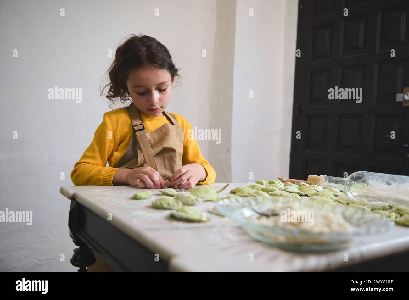 Caucasian charming child girl making dumplings in the home kitchen ...