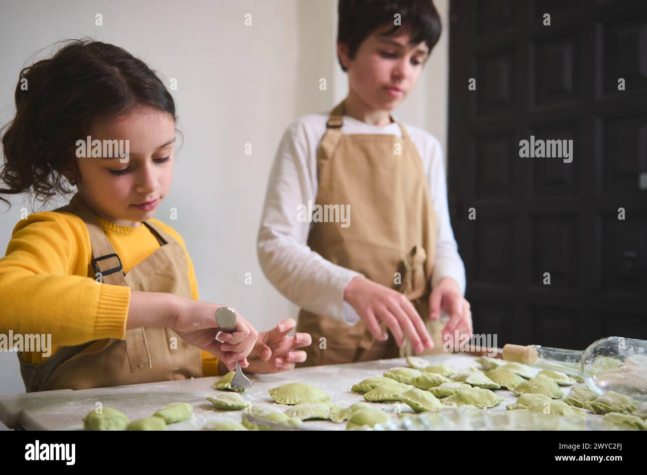 Brother and sister in beige chef's aprons, stuffing rolled dough rounds ...