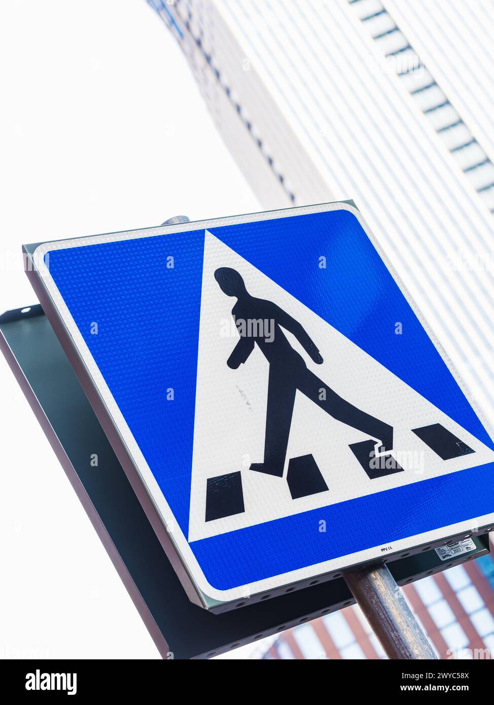 A pedestrian crossing sign stands prominently against a clear sky, with ...