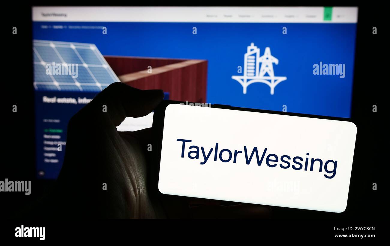 Person holding mobile phone with logo of international law company Taylor Wessing LLP in front ...