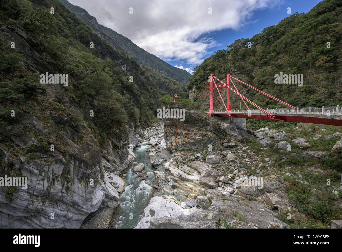 A red suspension bridge spans across a river cutting through deep rocky ...
