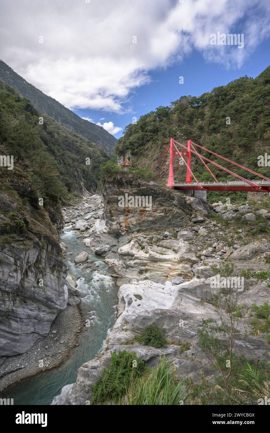 A red suspension bridge spans across a river cutting through deep rocky ...