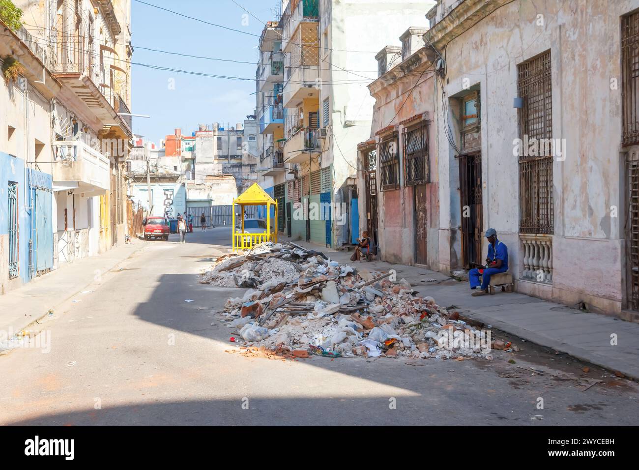 Cuban man sitting on sidewalk, pile of rubble on the city street in ...