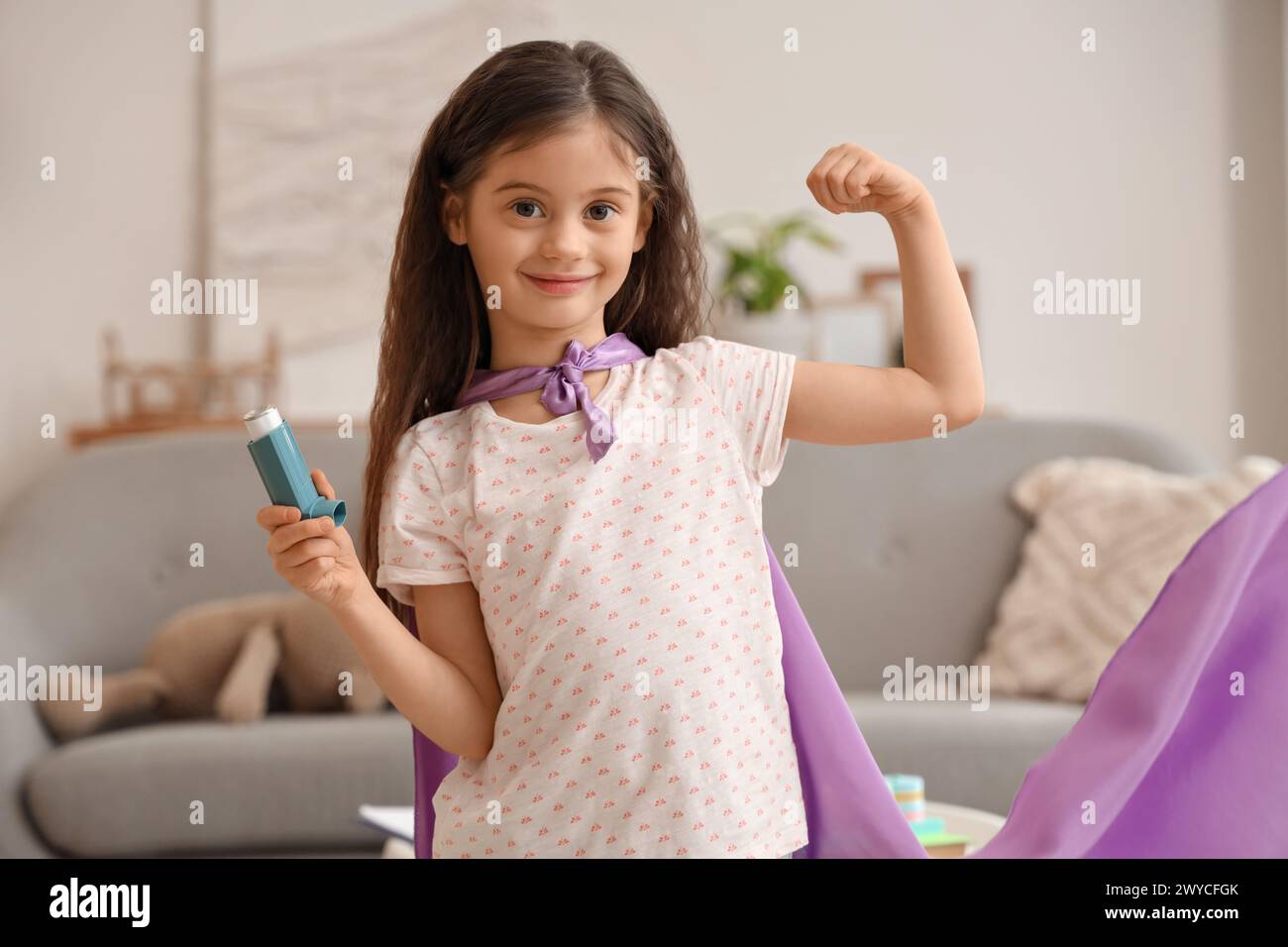 Little girl with superhero cape and inhaler showing muscles at home ...