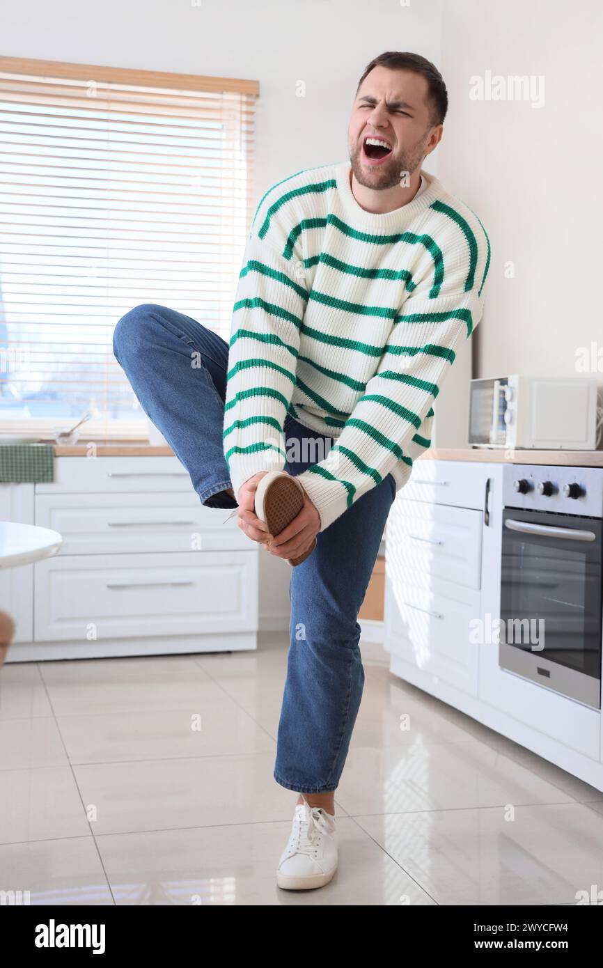 Young man suffering from pain in foot after tripping over table in ...