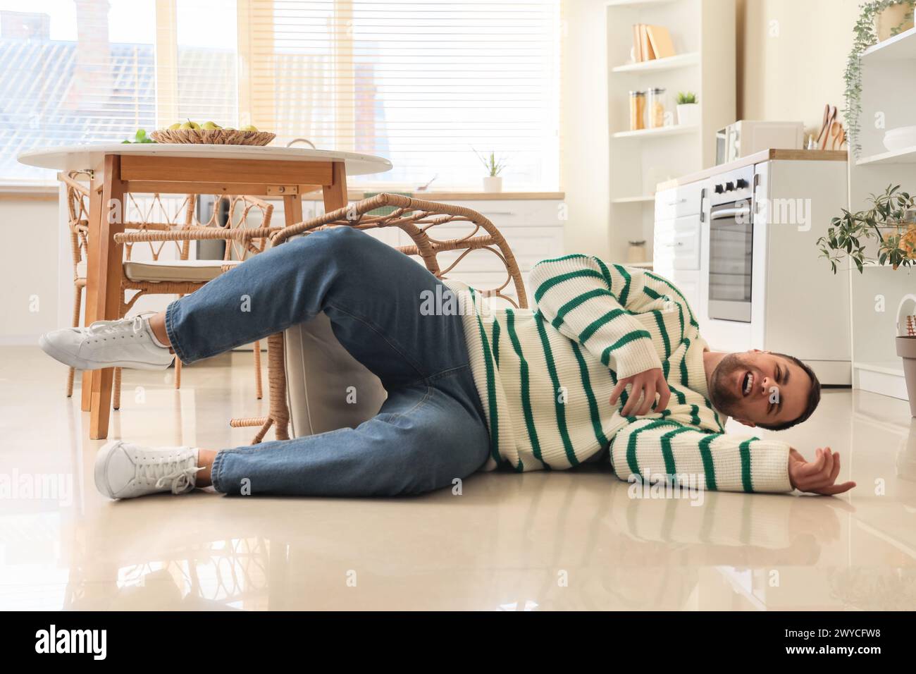 Young man lying on floor after falling from chair in kitchen Stock ...