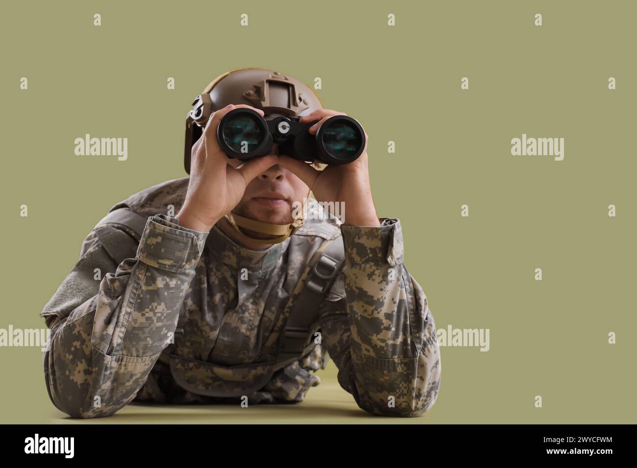 Lying male soldier in uniform looking through binoculars on green ...