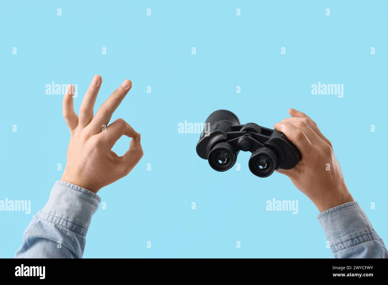 Male hands with binoculars showing OK on blue background Stock Photo ...
