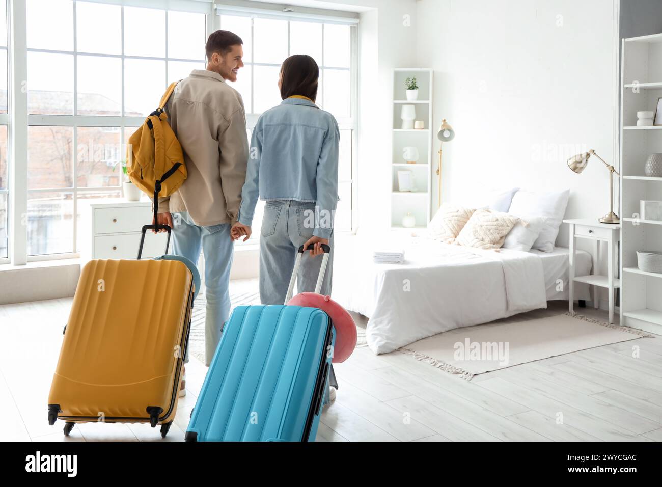 Young couple of tourists with bags checking in hotel room, back view ...