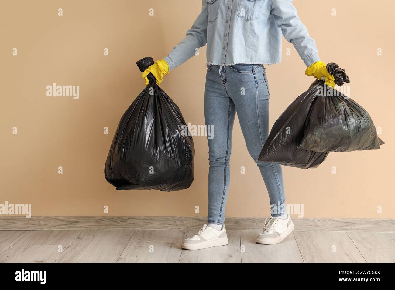 Woman with garbage bags near beige wall Stock Photo - Alamy