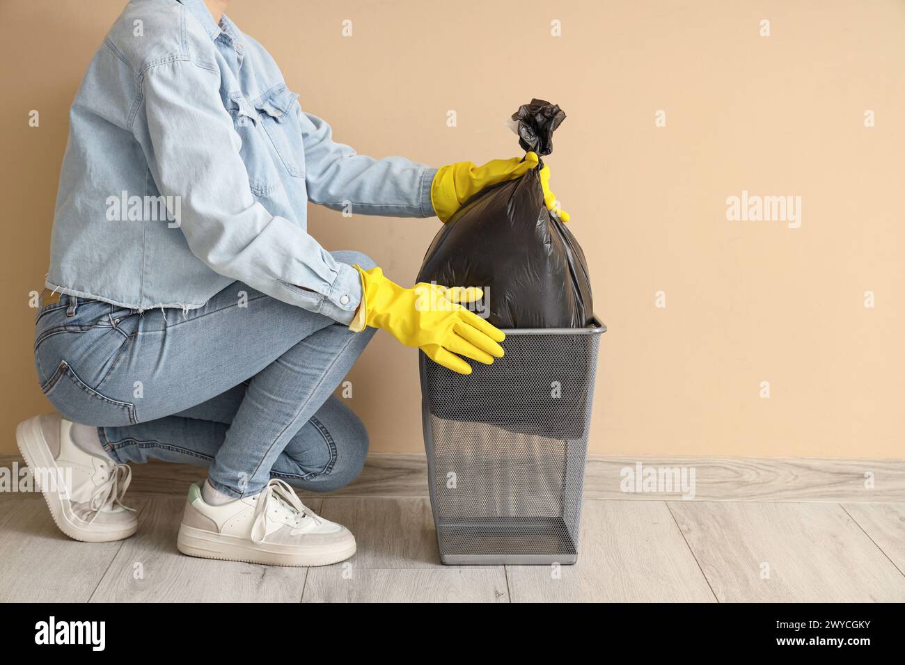 Woman taking garbage bag from trash bin near beige wall Stock Photo - Alamy