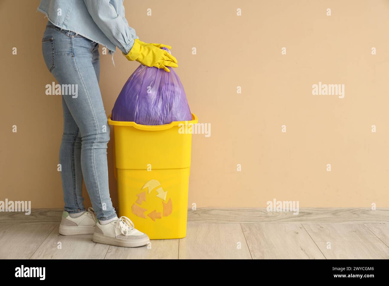 Woman taking garbage bag from trash bin near beige wall Stock Photo - Alamy